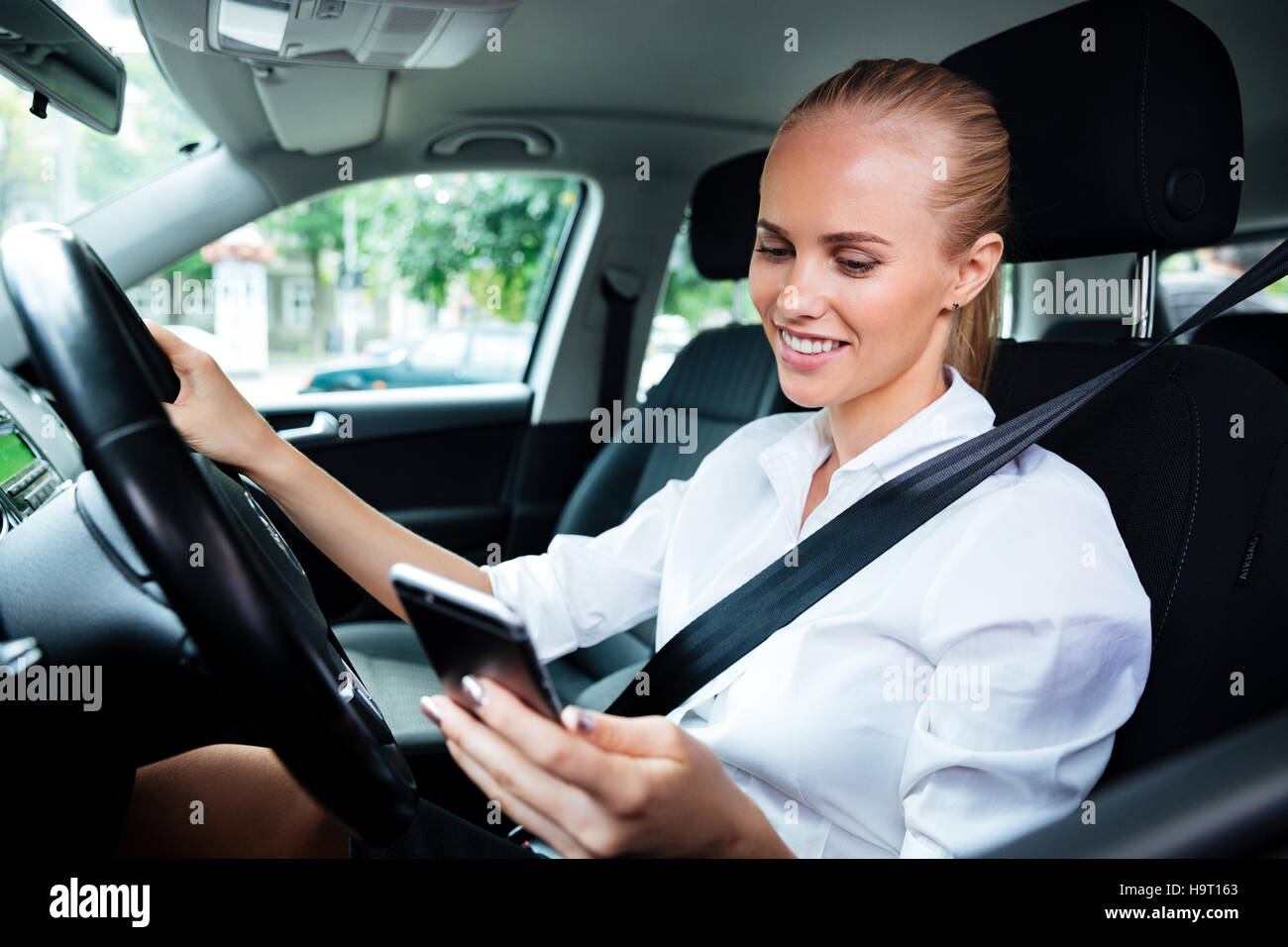 Smiling young business woman dialing phone number while driving car ...