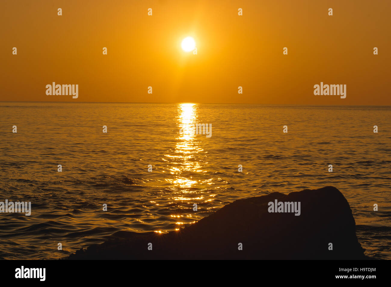 a Vivid orange sunset over water, with rock silhouettes. Thailand ...