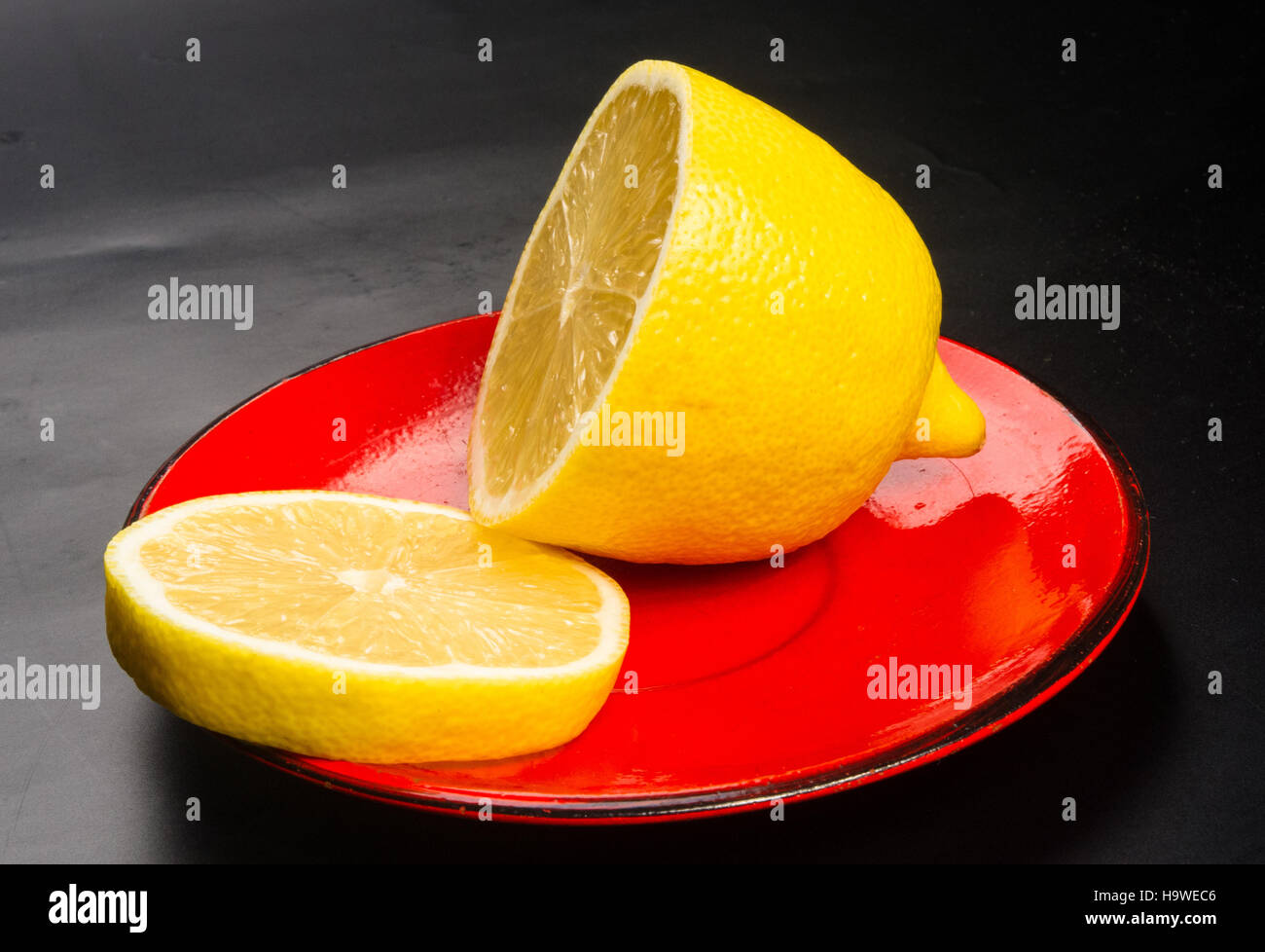 Sliced yellow lemon in red saucer on black background Stock Photo - Alamy