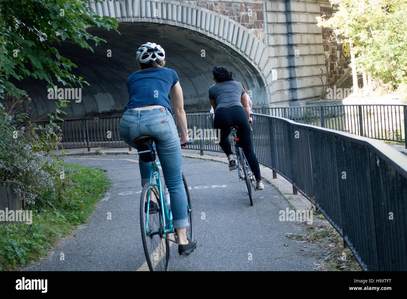 two woman riding bicycles under bridge by channel between Lake Calhoun ...