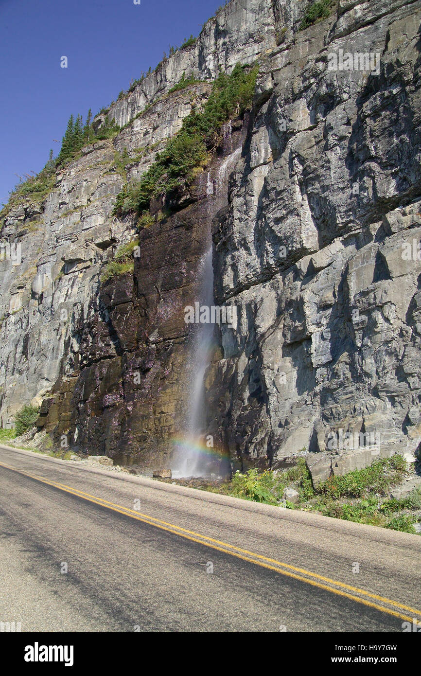 A waterfall at Glacier National Park flows directly onto the road ...