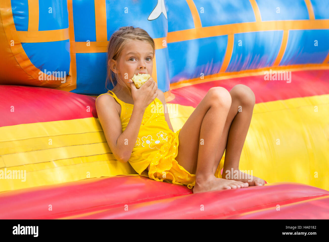 Girl sits at the entrance to an inflatable trampoline and eating an ...