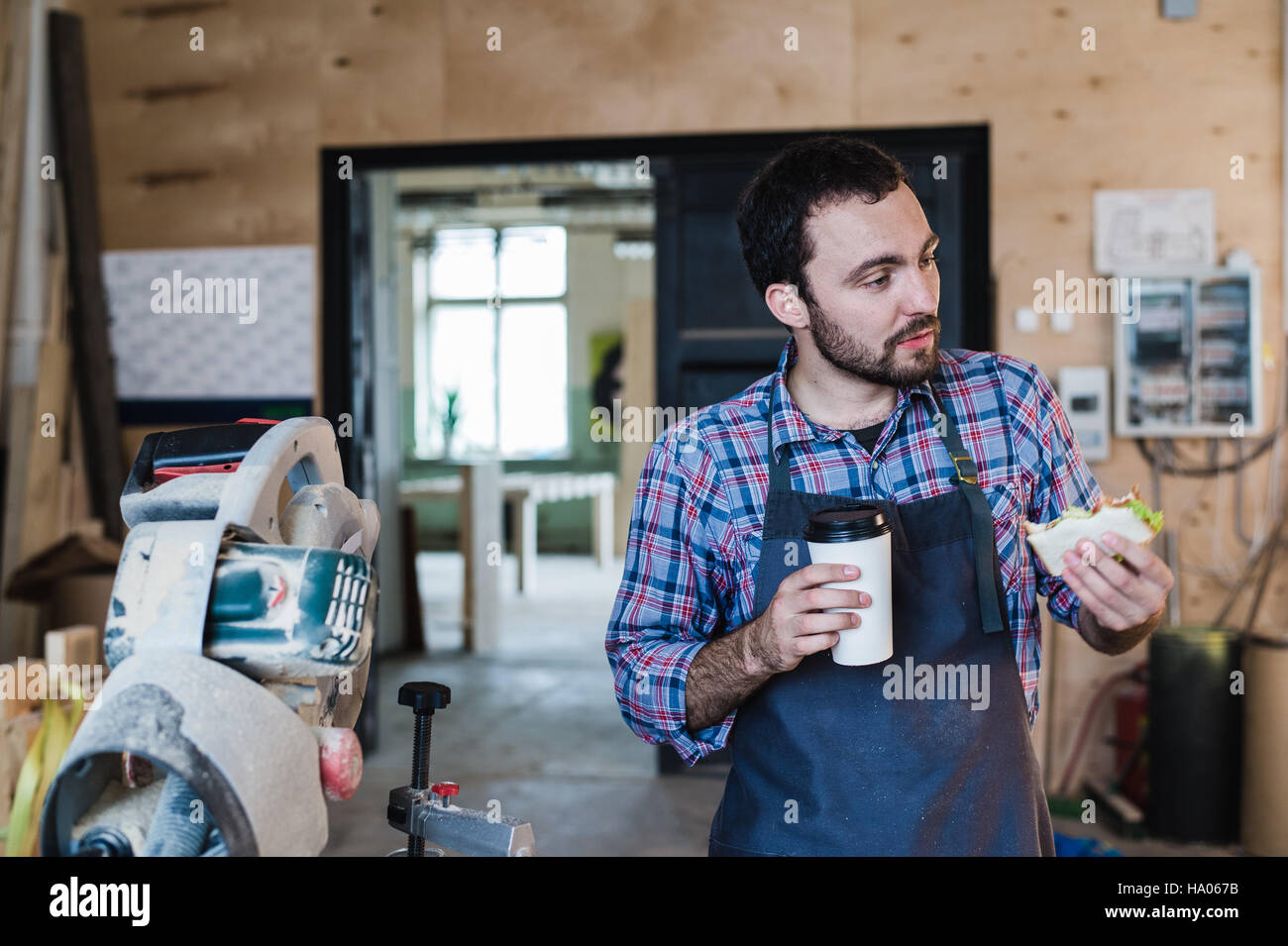 Cheerful carpentry worker having lunch eating sandwich in a workshop ...