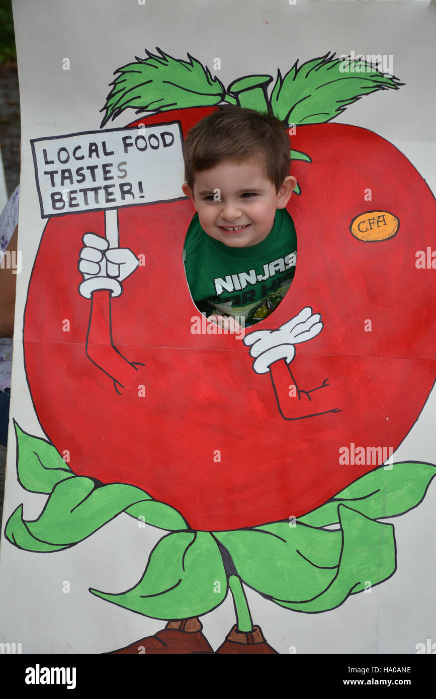 A child smiles while peeking out from behind a 'Local Food Tastes ...