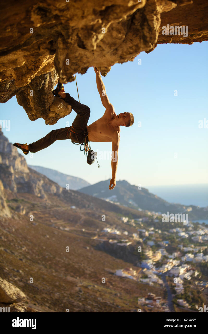 Young man climbing on roof of cave against view of coast below Stock ...