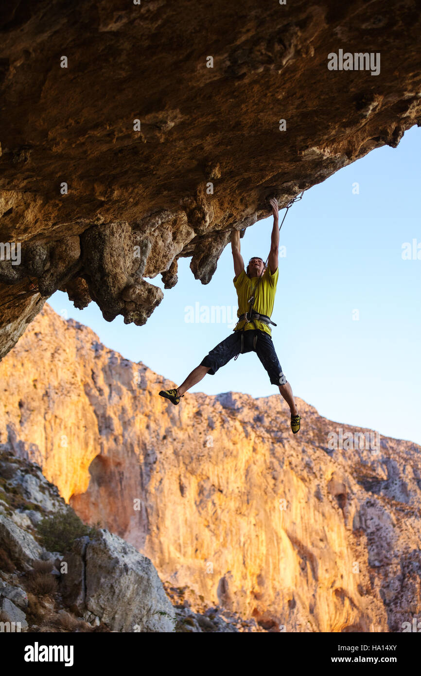 Male rock climber hanging on roof of cave while climbing Stock Photo ...