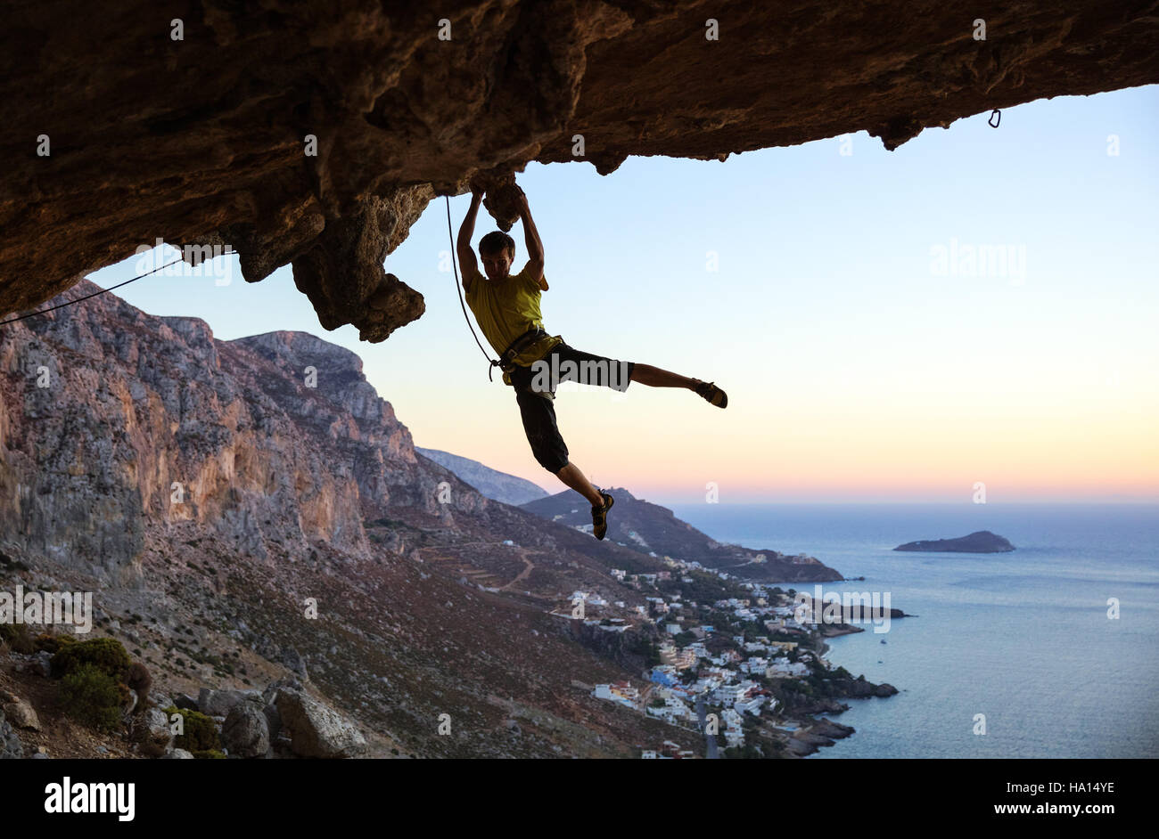 Rock climber jumping on handholds while climbing overhanging cliff ...