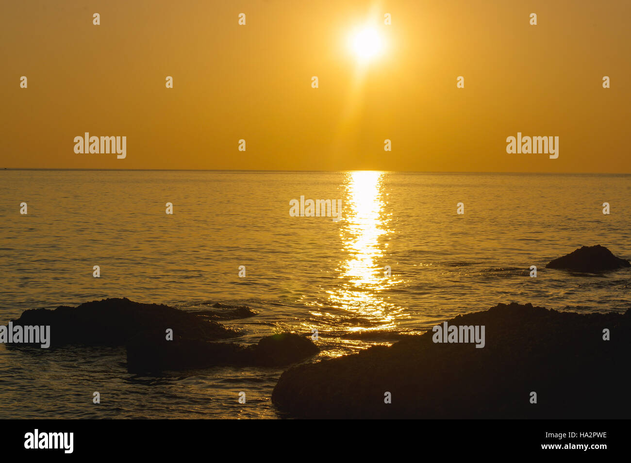 a Vivid orange sunset over water, with rock silhouettes. Thailand ...