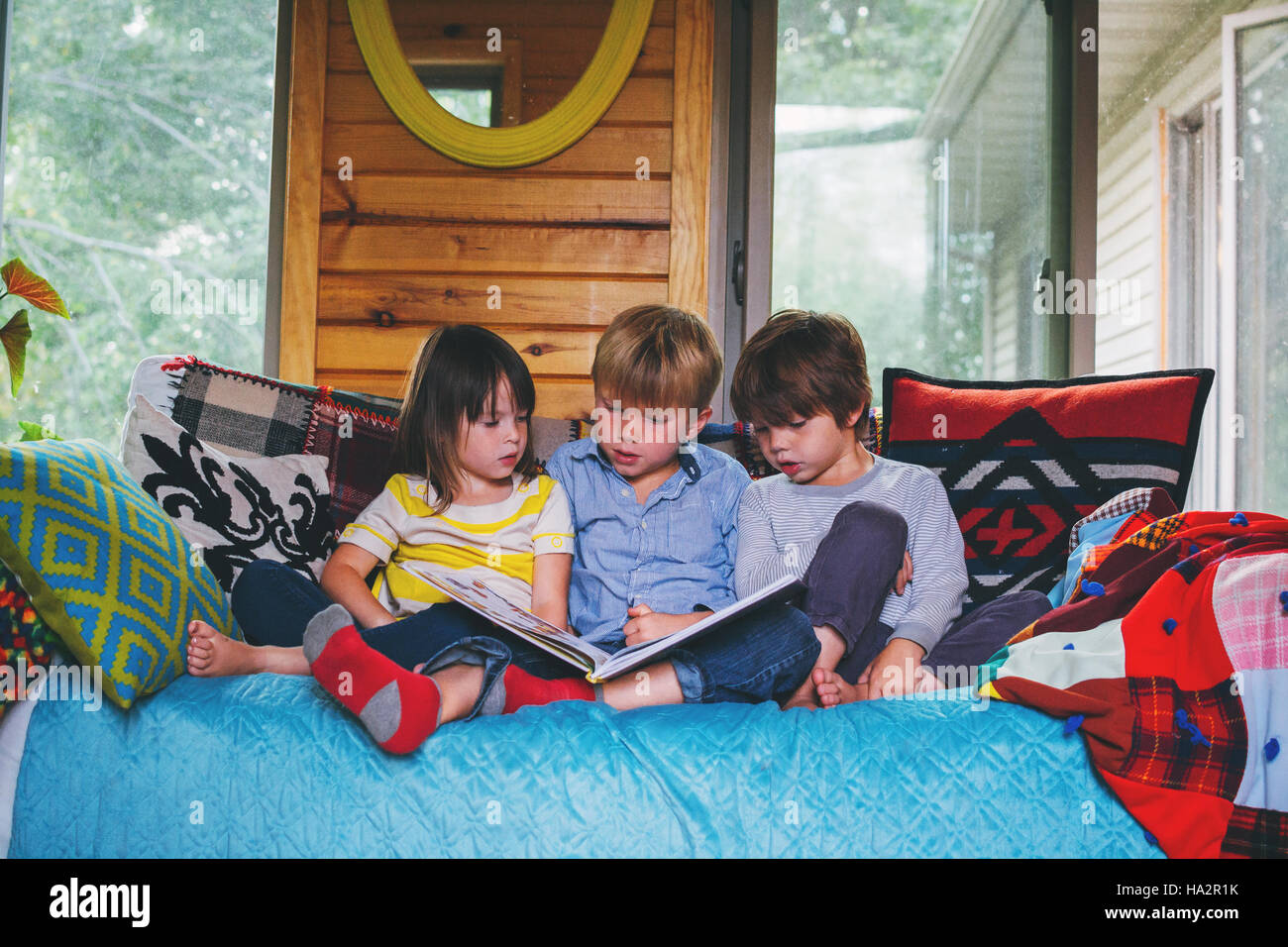 Three children sitting on couch reading Stock Photo - Alamy