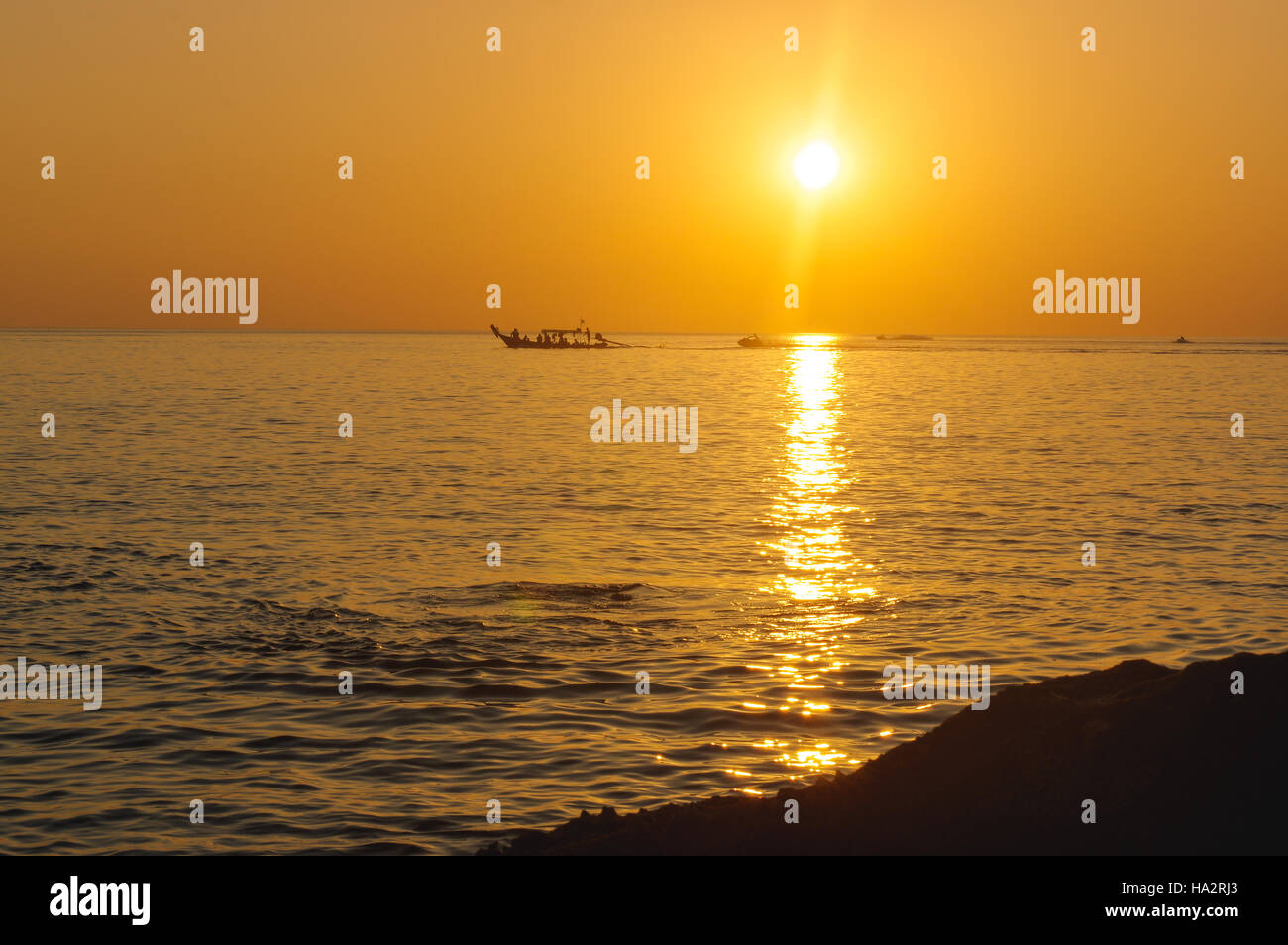 a Vivid orange sunset over water, with rock silhouettes. Thailand ...