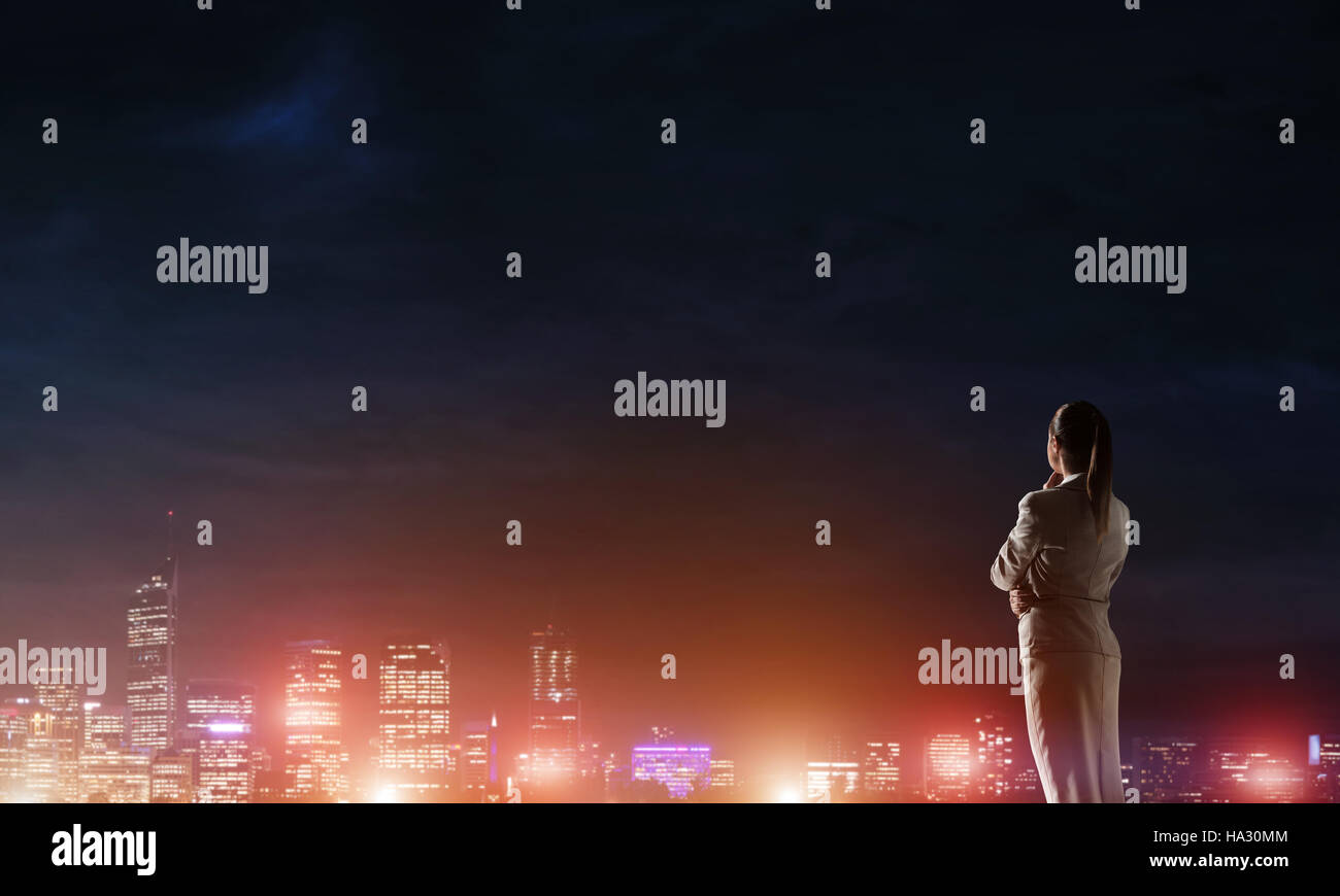 Rear view of elegant businesswoman viewing lights of night city Stock ...