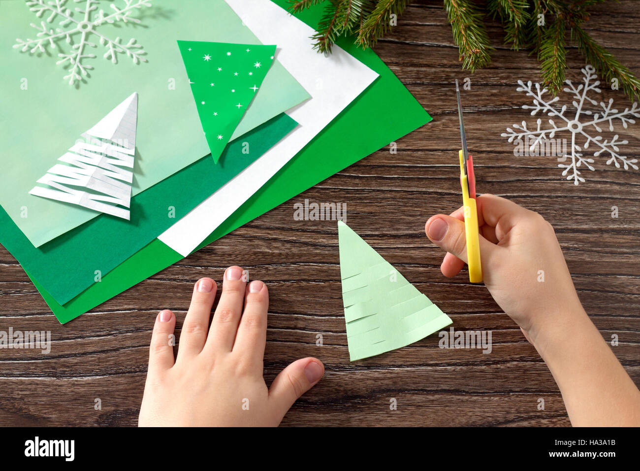 The child makes paper fir tree. Scissors, paper on a wooden table ...