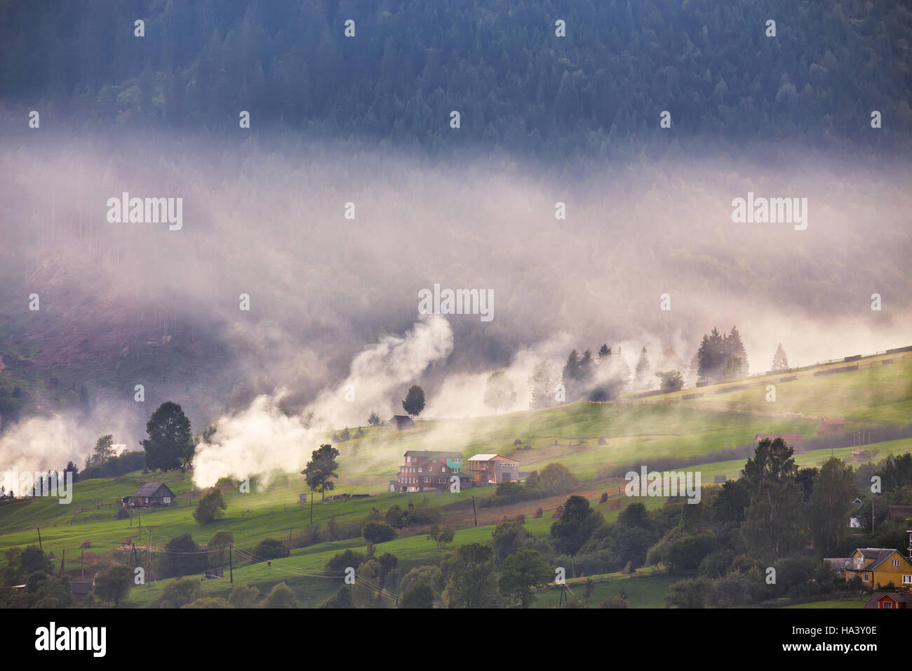 Alpine village in mountains. Smoke, bonfire and haze over the hills in ...