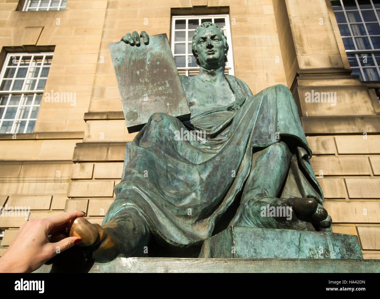 A tourist touches the big toe of the statue of philosopher David Hume ...