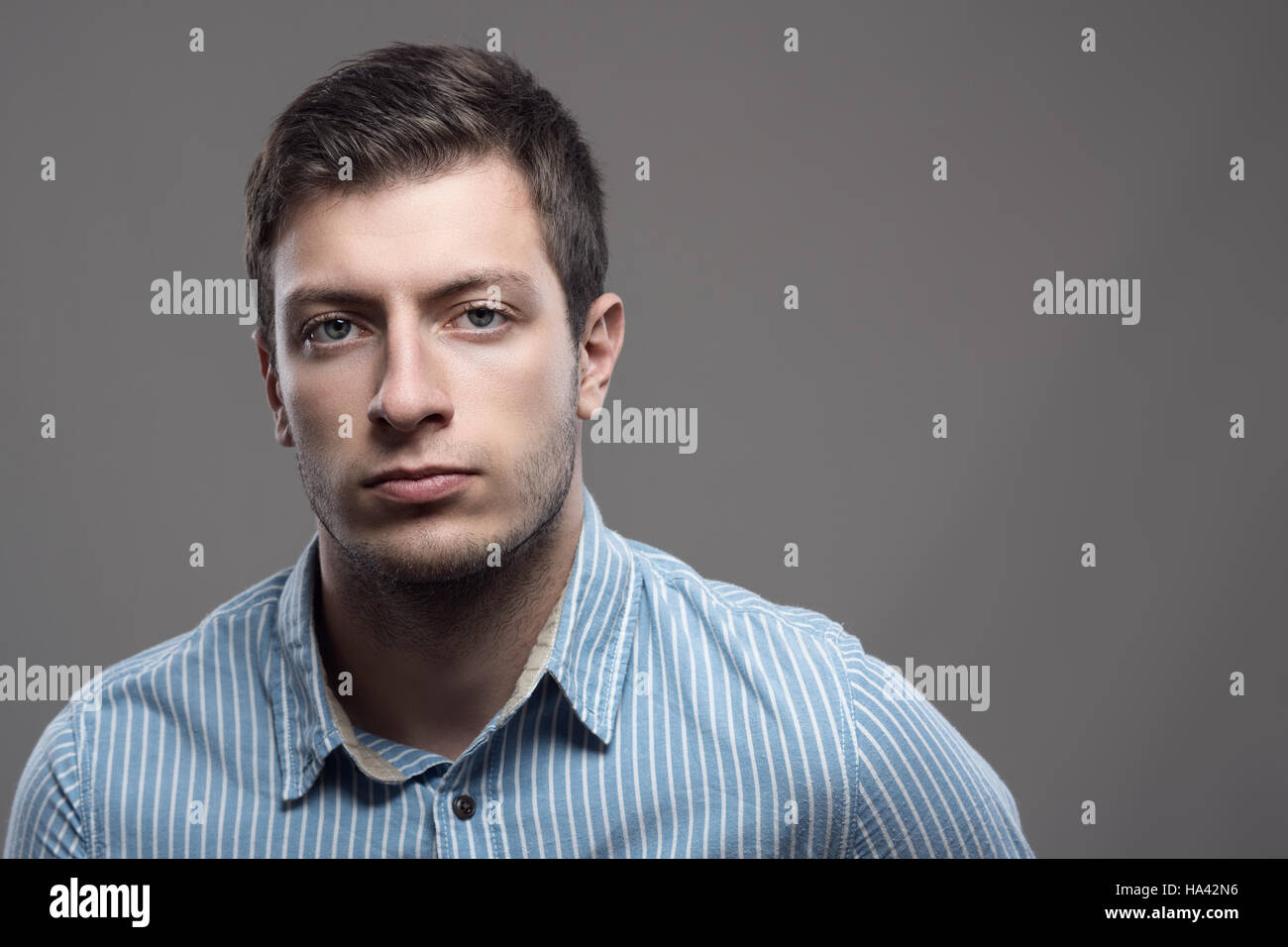 Moody dramatic portrait of serious young man in blue shirt looking at ...