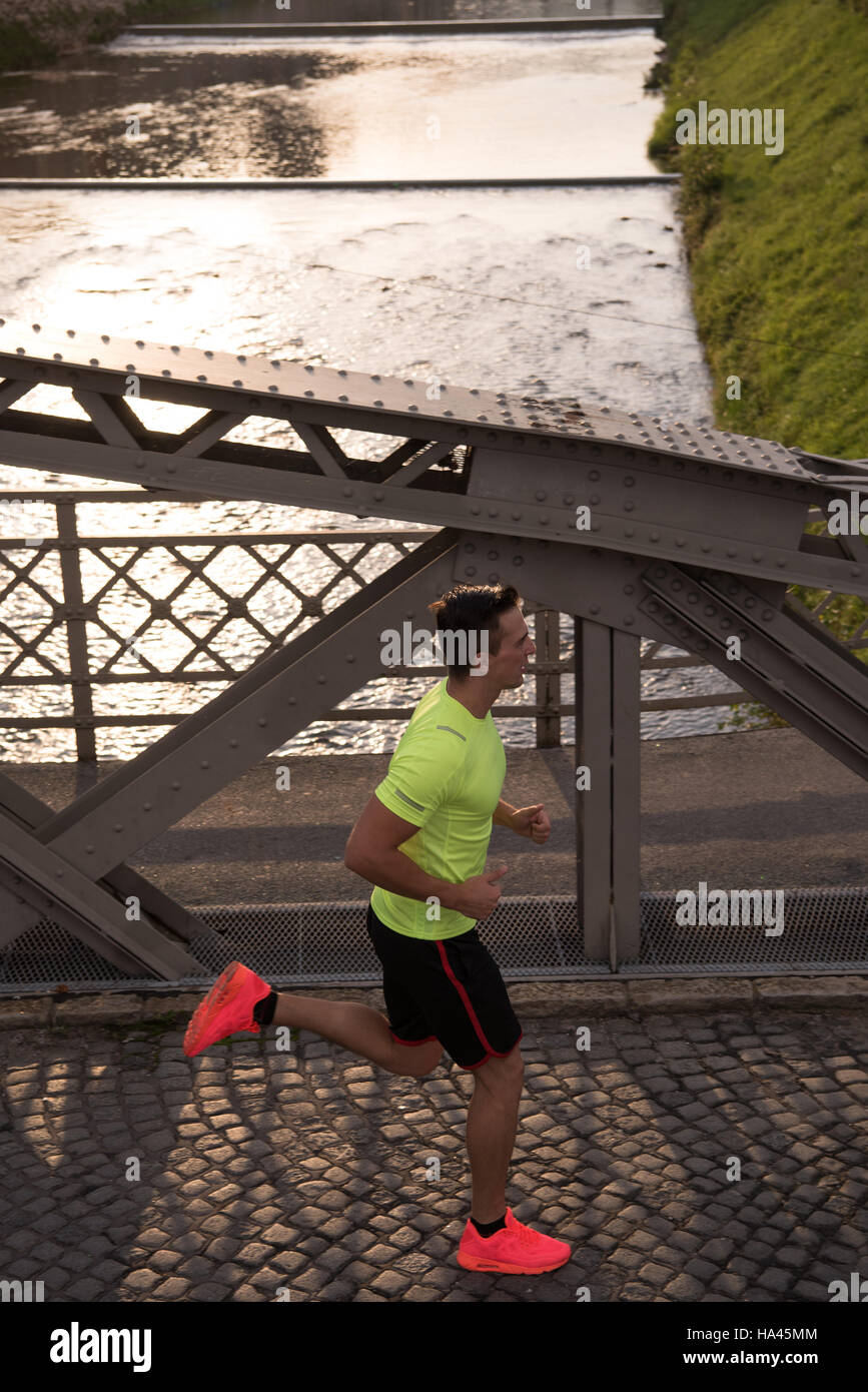 Young sporty man running on sidewalk at early morning jogging with city ...