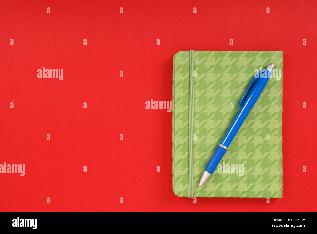 Green notebook with blue pen isolated on red background with soft ...