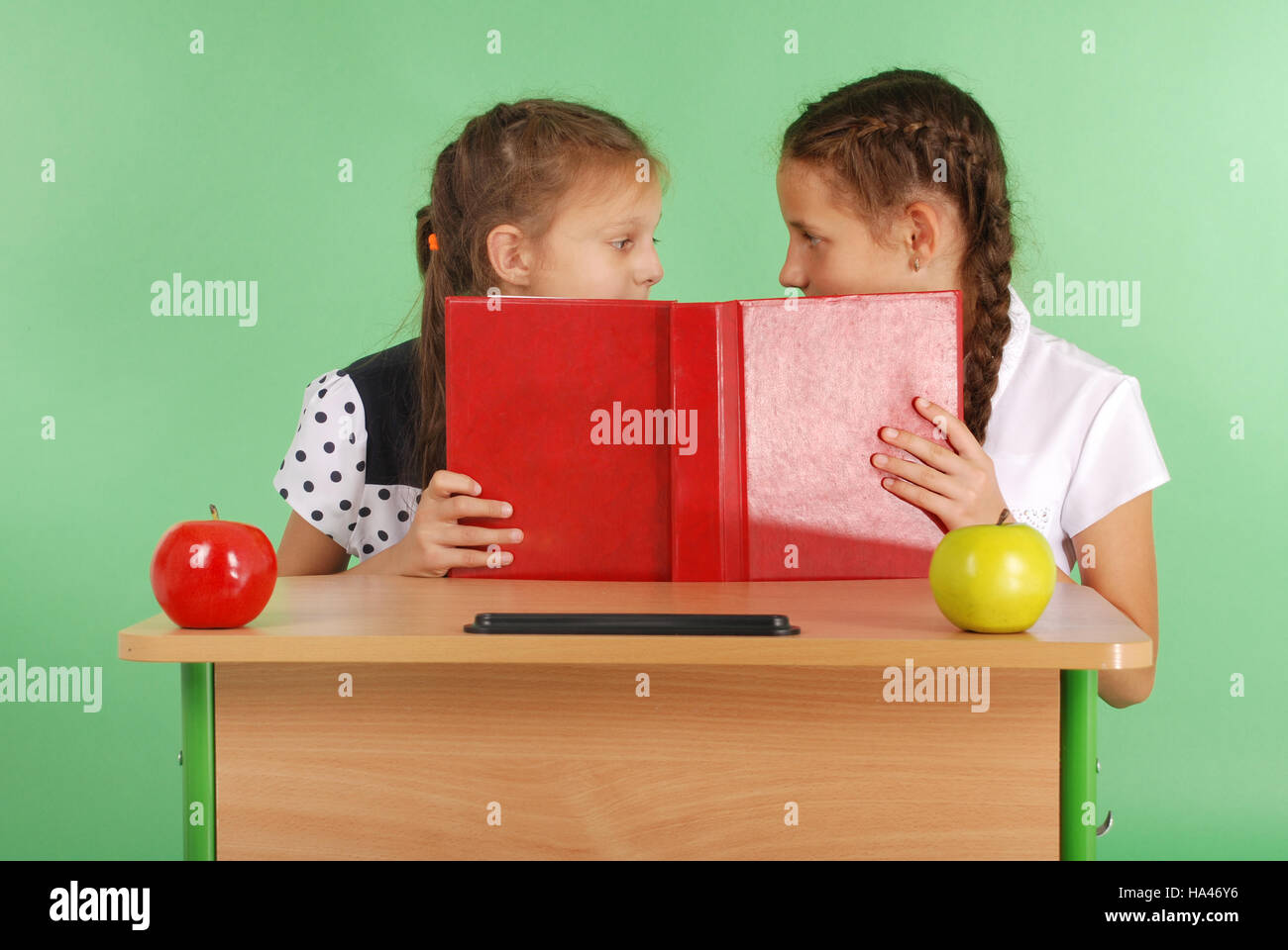 Two school girl sharing secrets sitting at a desk from book isolated on ...