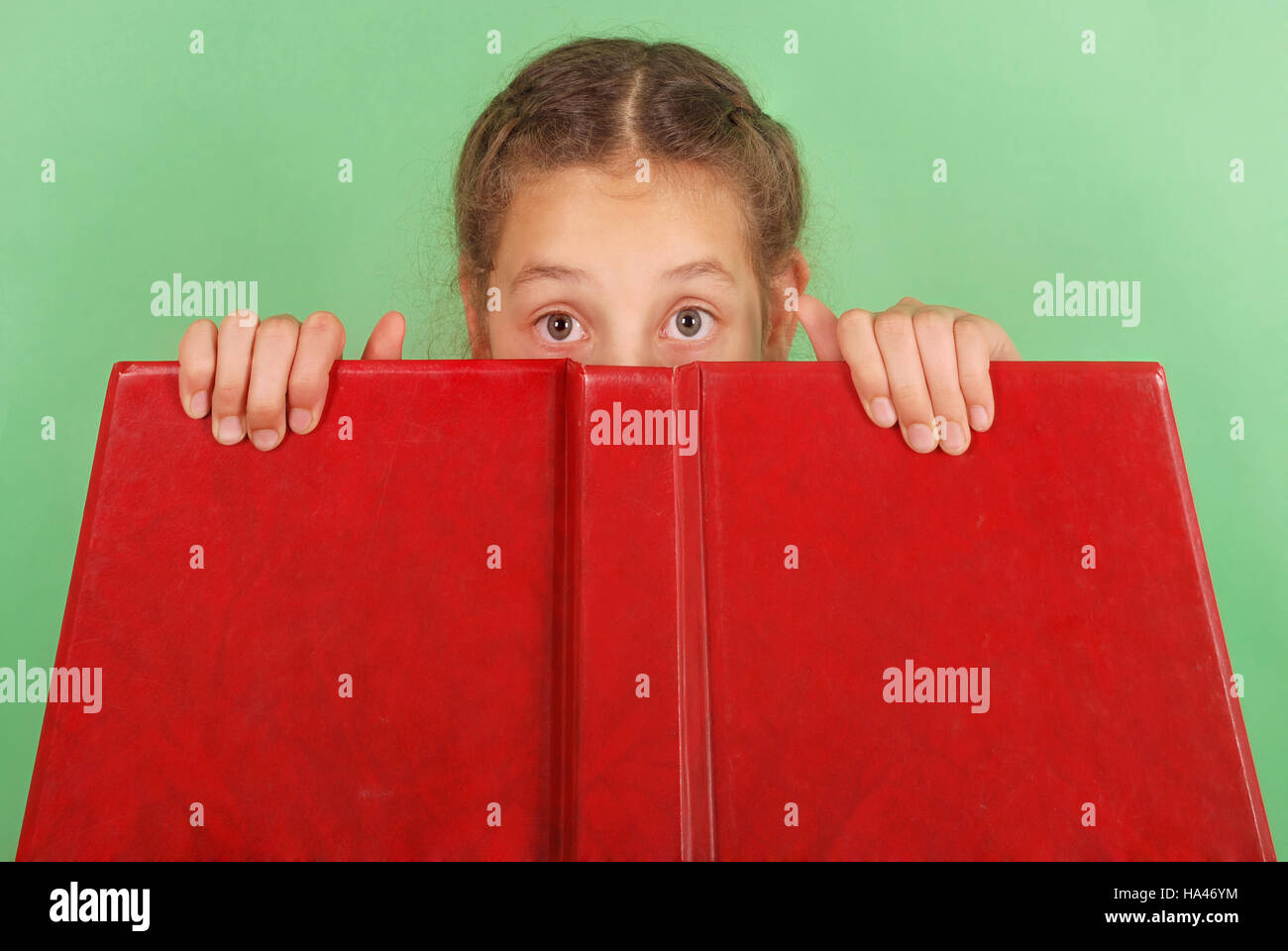 Beautiful school girl peeping from behind her red book isolated on ...