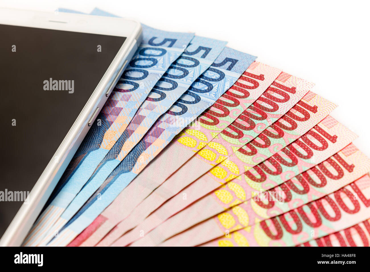 Smartphone above the piles of Indonesian Rupiah (IDR) banknotes on the ...