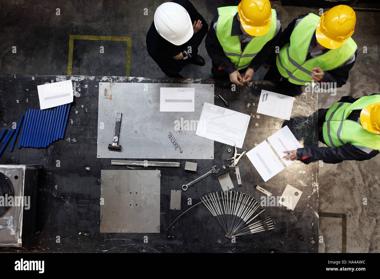 Workers and manager in safety helmets working with documents at factory ...