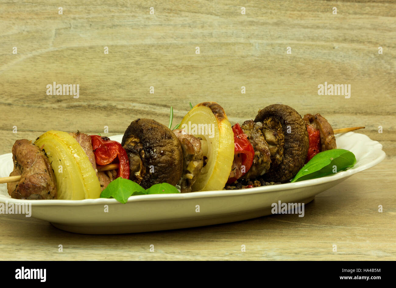 Close view from side on a skewer sirloin beef on white dish with onion ...
