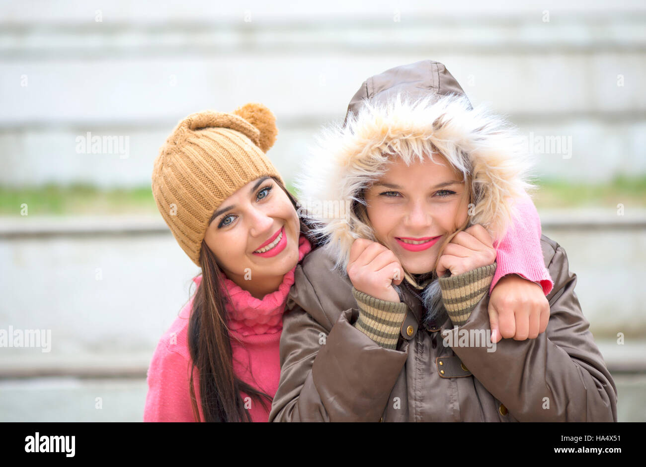 Two cheerful cute girls, one hugging her best female friend outdoors in ...