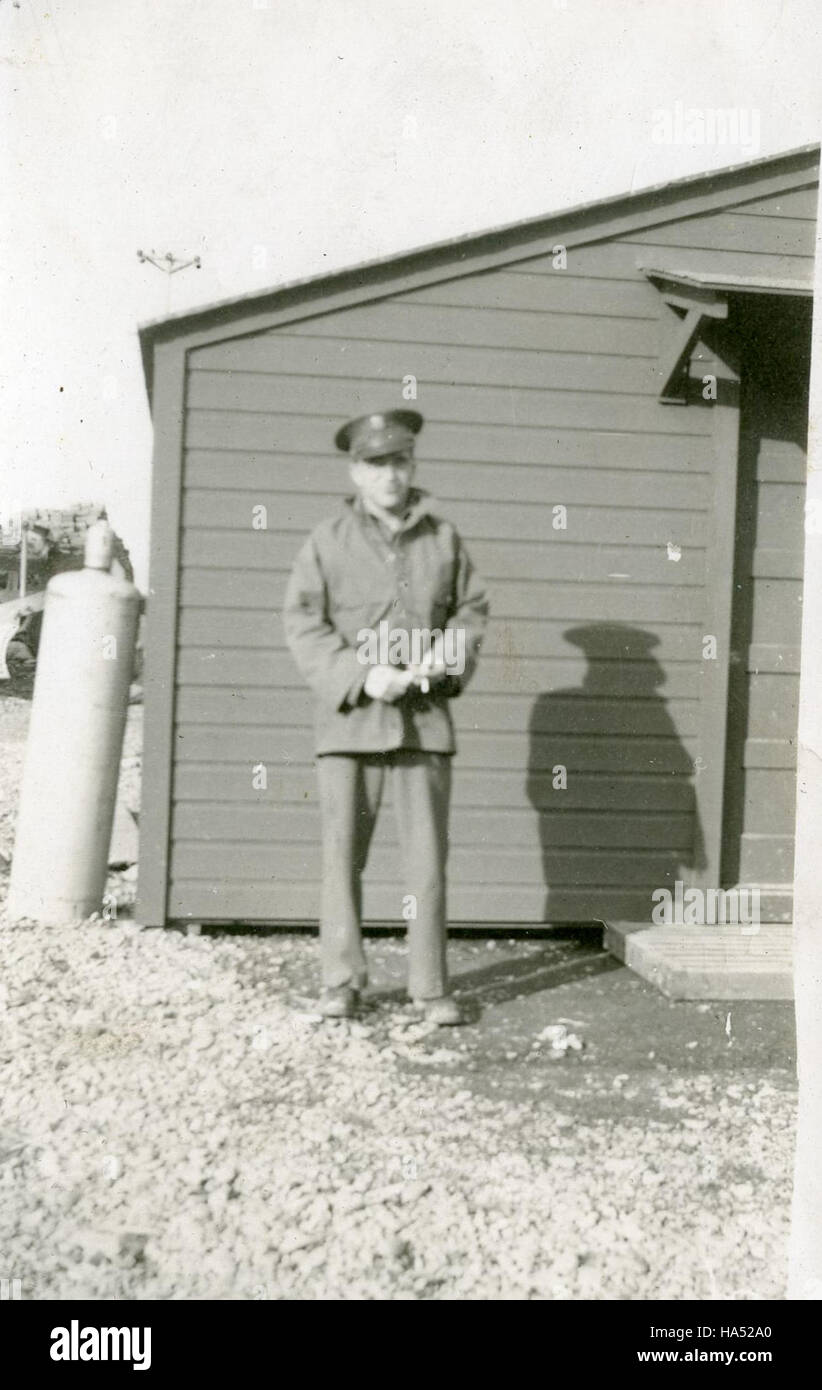 A historical photograph showing a uniformed individual near barracks in ...