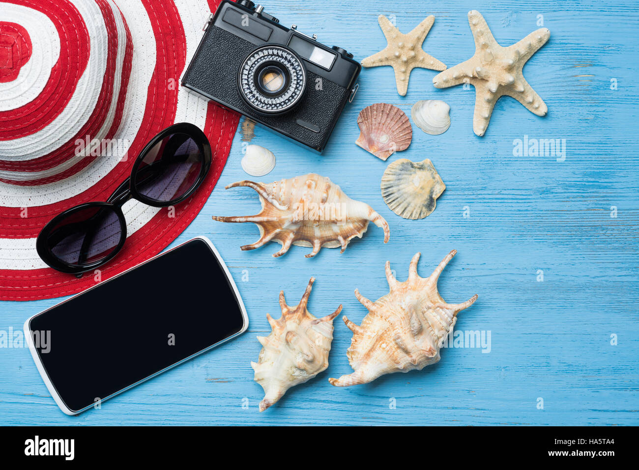 Straw hat sunglasses smartphone and photocamera among sea shells and ...