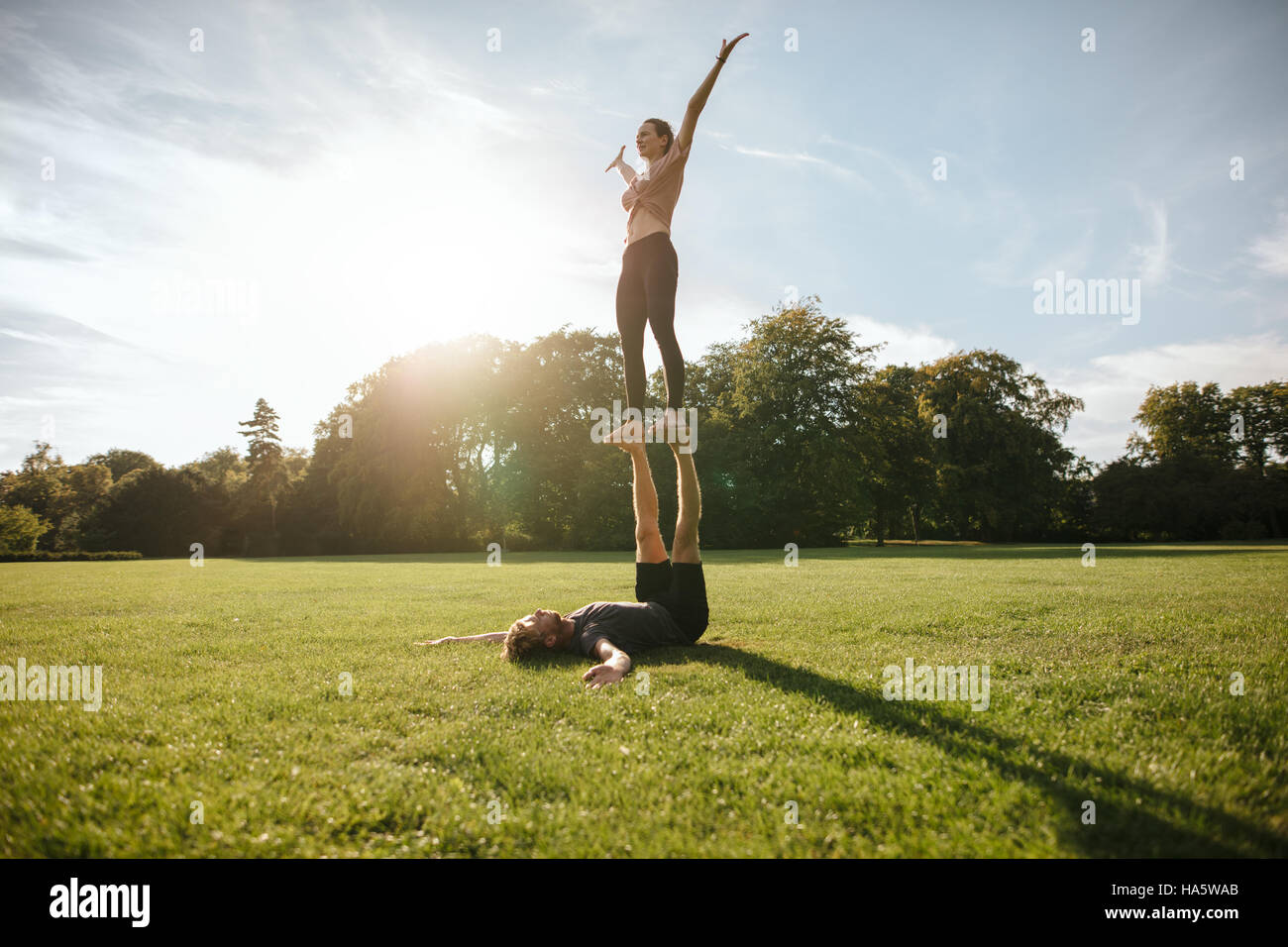 Outdoor shot of couple doing acrobatic yoga exercise at park. Young man ...