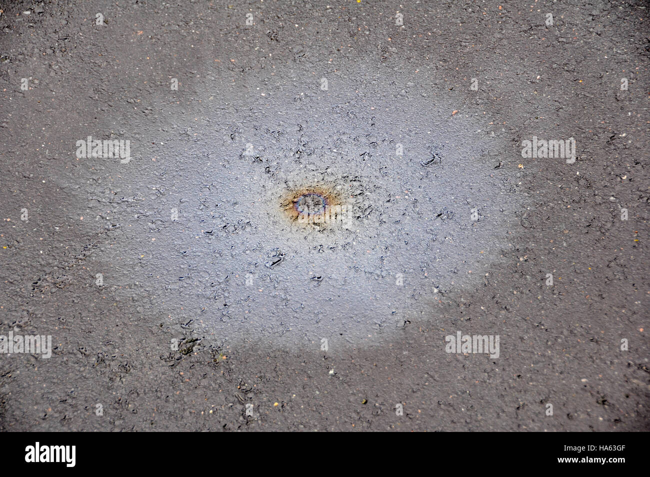 A single oil drip from a V8 engine spreads on wet tarmac to create ...