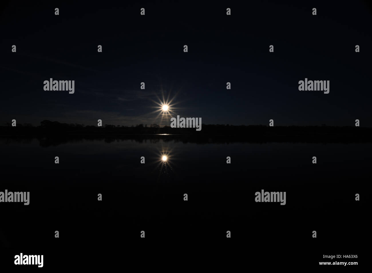 Starry sun reflects in calm water at low tide making a silhouette with ...