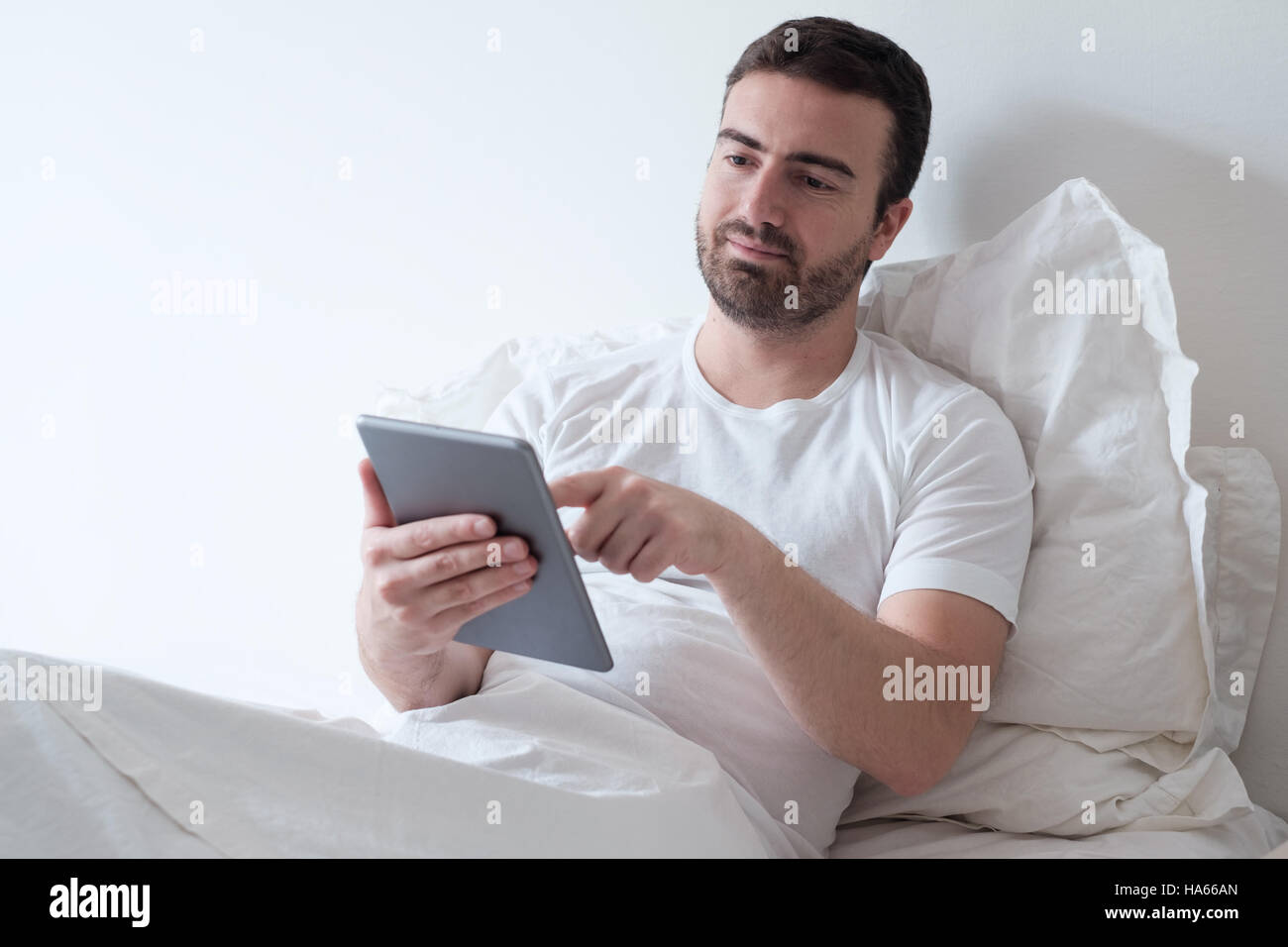 Man using his electronic tablet lying in the bed Stock Photo - Alamy