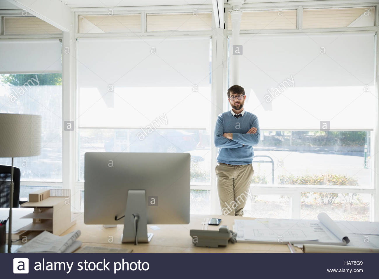 Portrait confident male architect with arms crossed at office window ...