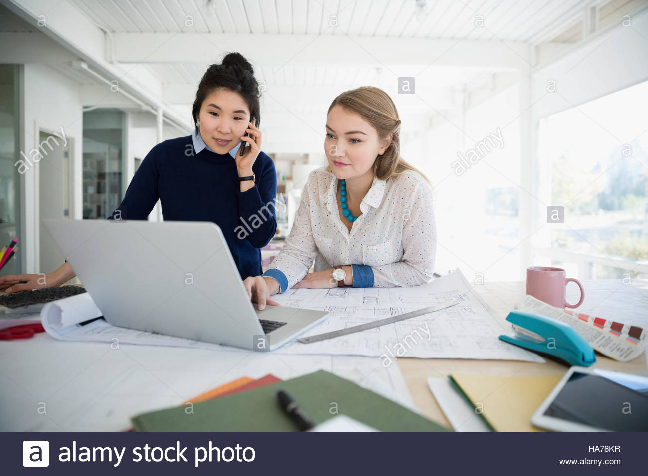 Female architects using laptop and talking on cell phone in office ...