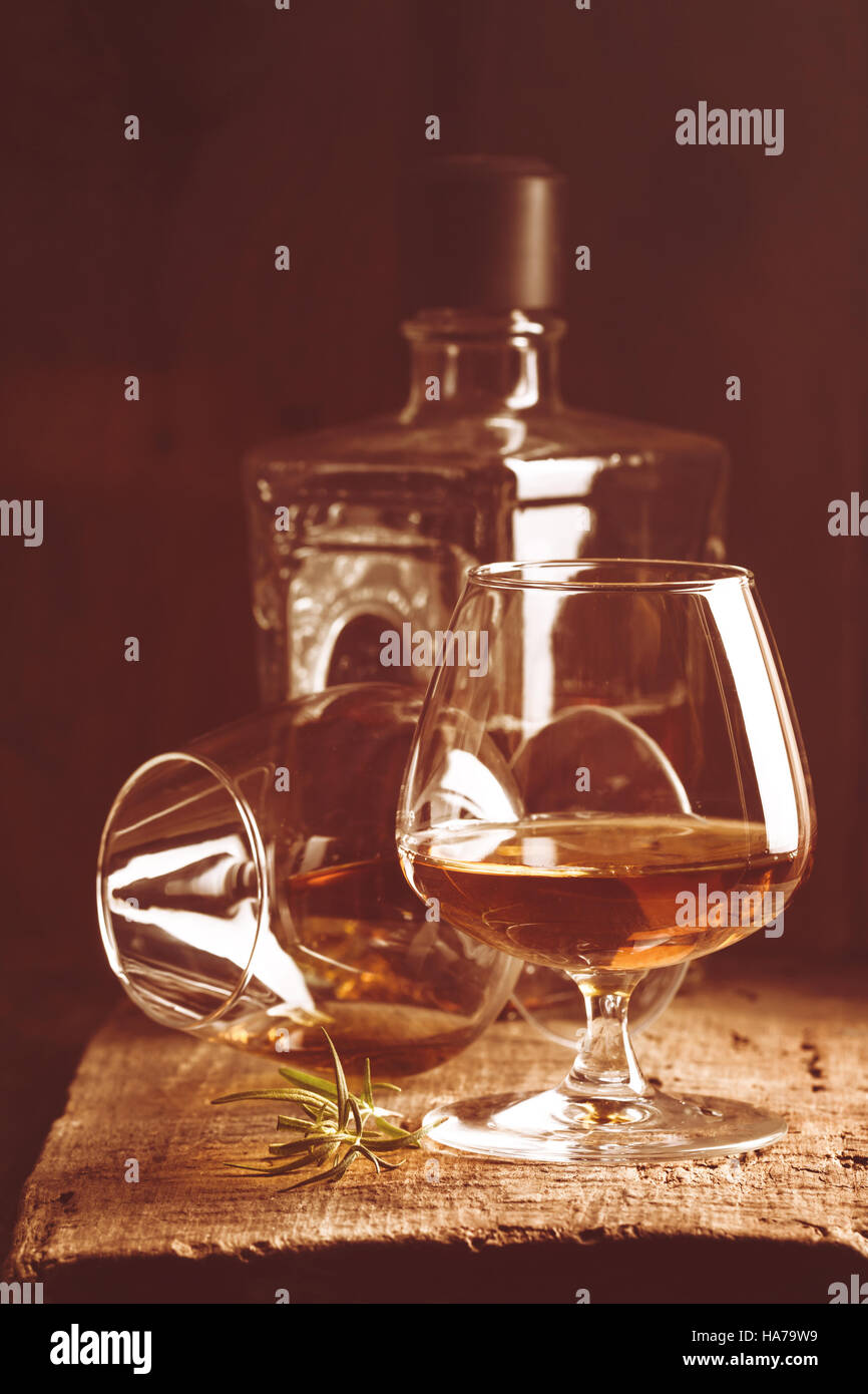 Glass of brandy or cognac and bottle on old oak wooden table. Dark ...