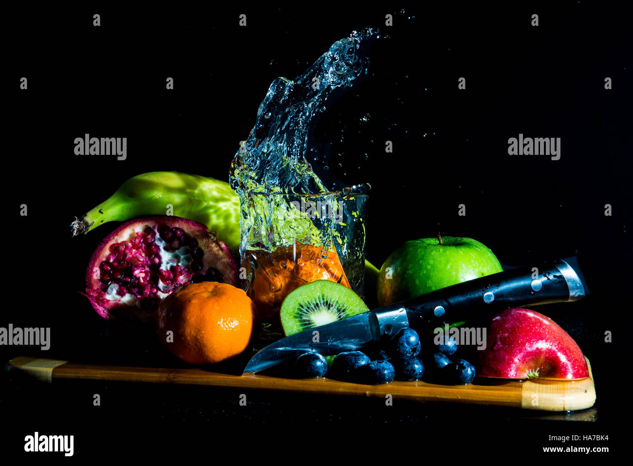 Low key image of a plate of fruits arranged around a glass of water ...