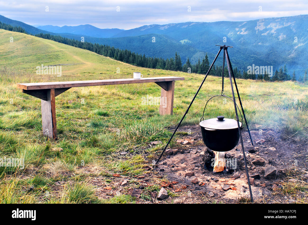 Camping fire and tourists bowler with preparing food in mountains ...
