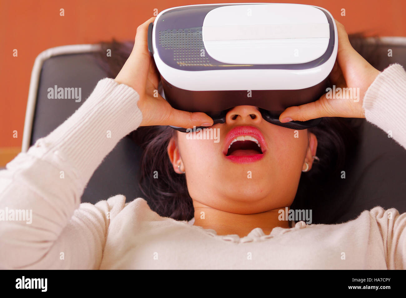 Young brunette woman lying down wearing virtual reality goggles ...