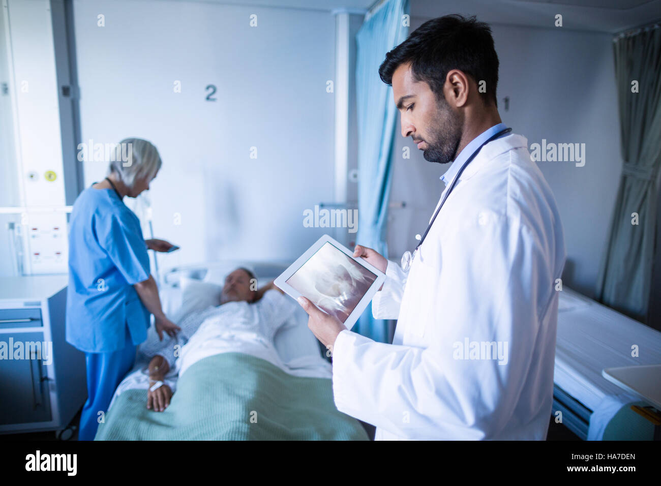 Doctor looking at digital tablet while nurse assisting a patient in ...
