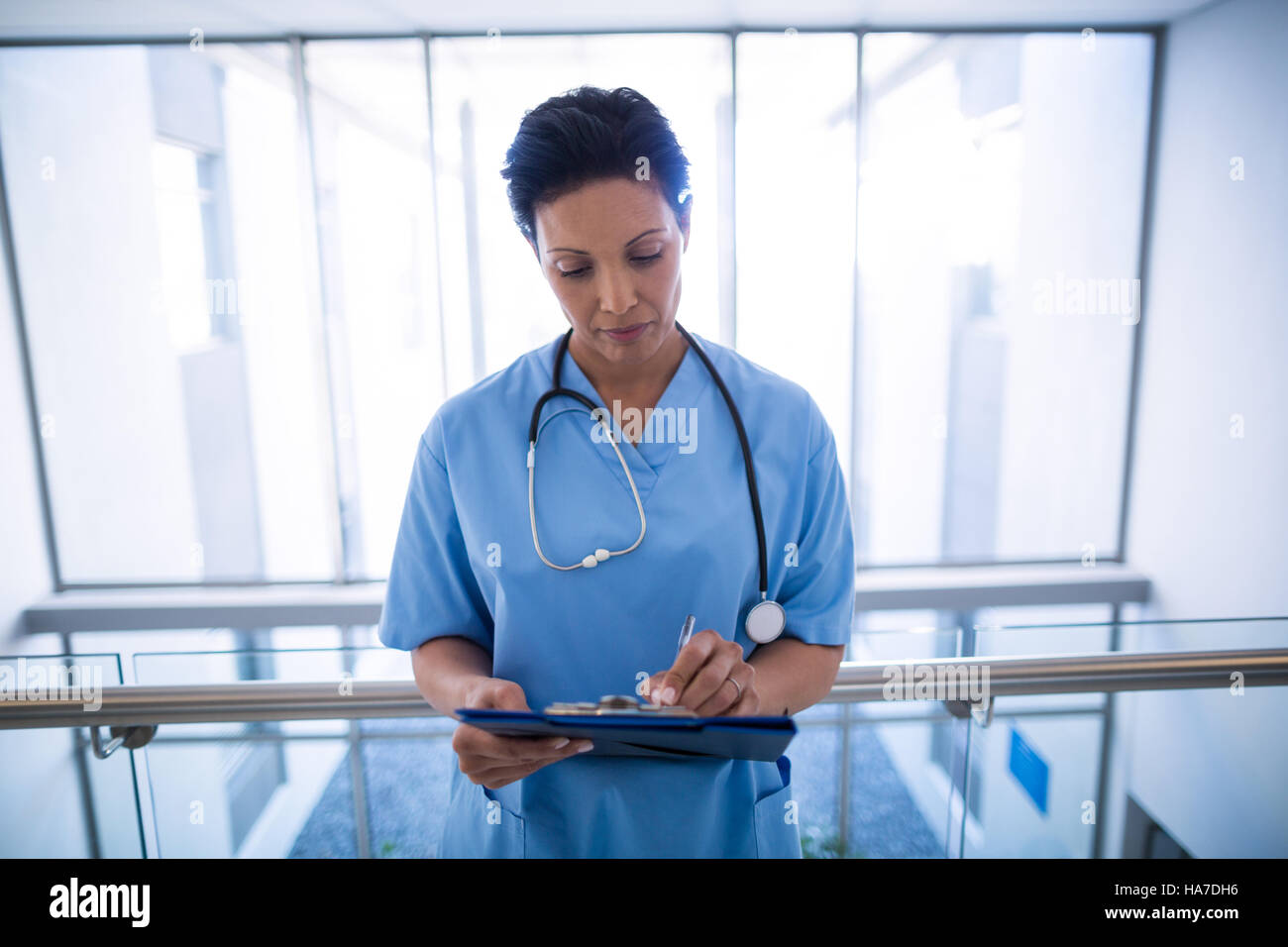 Female nurse writing in clipboard in corridor Stock Photo - Alamy
