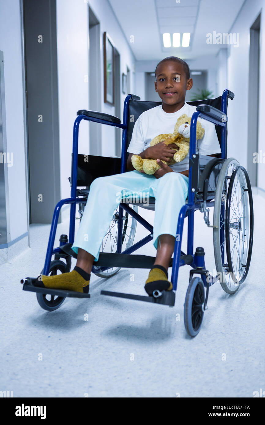 Portrait of boy sitting on wheelchair and holding teddy bear in ...