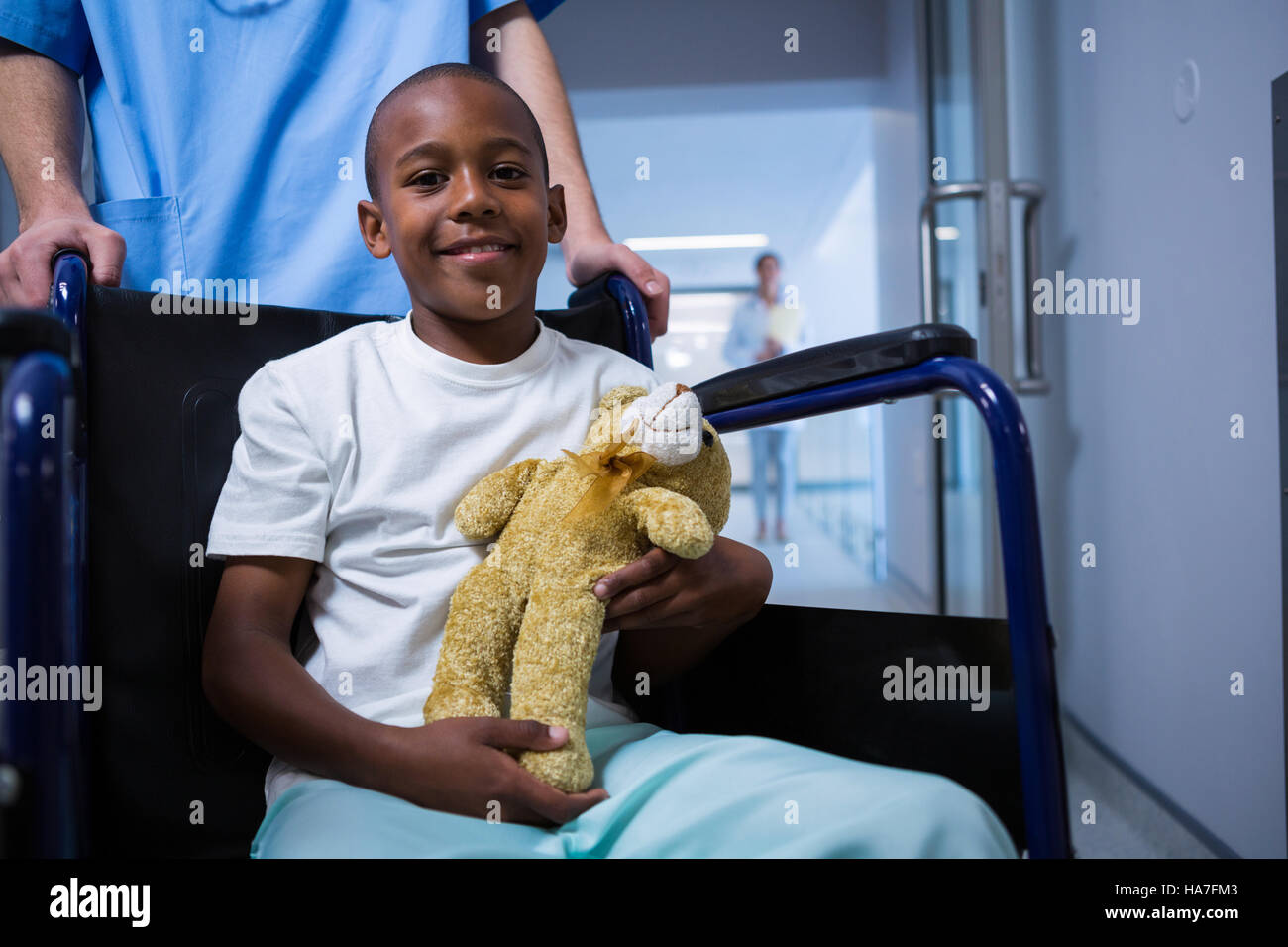 Portrait of boy sitting on wheelchair and holding teddy bear in ...