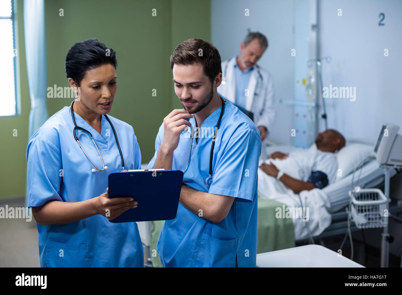 Male and female nurse having discussion over clipboard in ward Stock ...