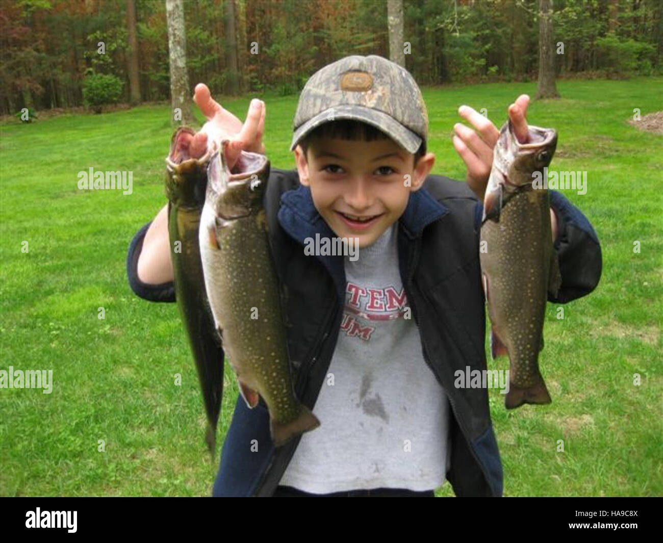 A young boy smiles proudly with a trout he caught, showcasing the ...