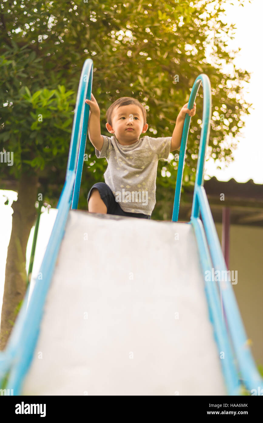 Little Asian kid playing slide at the playground under the sunlight in ...