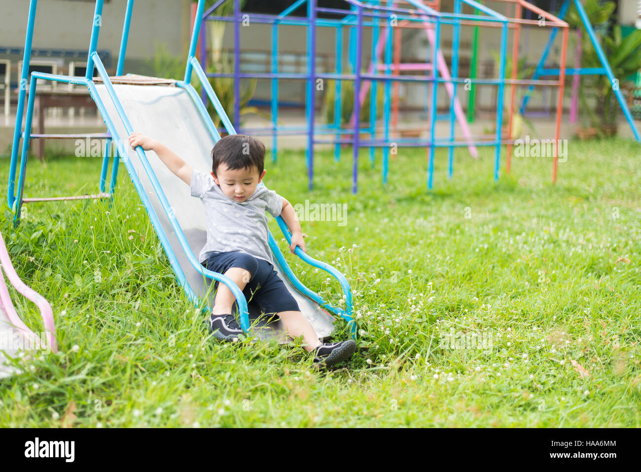 Little Asian kid playing slide at the playground under the sunlight in ...