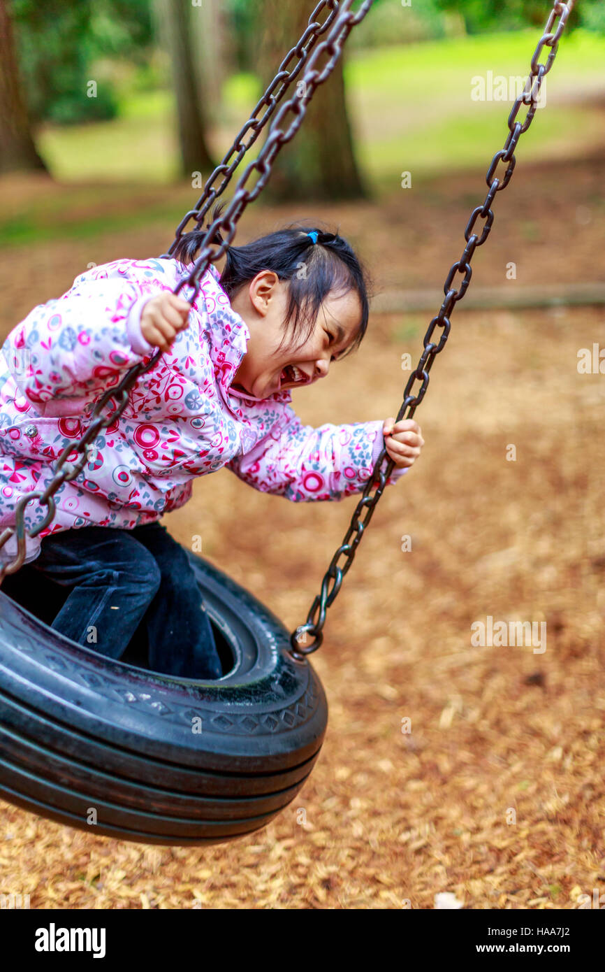Adorable little girl having a great time on a swing in the playground ...
