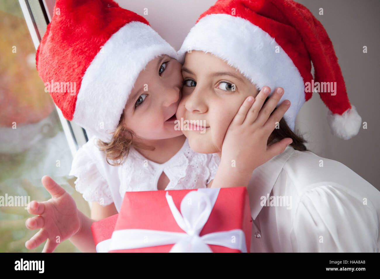 little girl in Santa hat kissing older sister with a gift Stock Photo ...