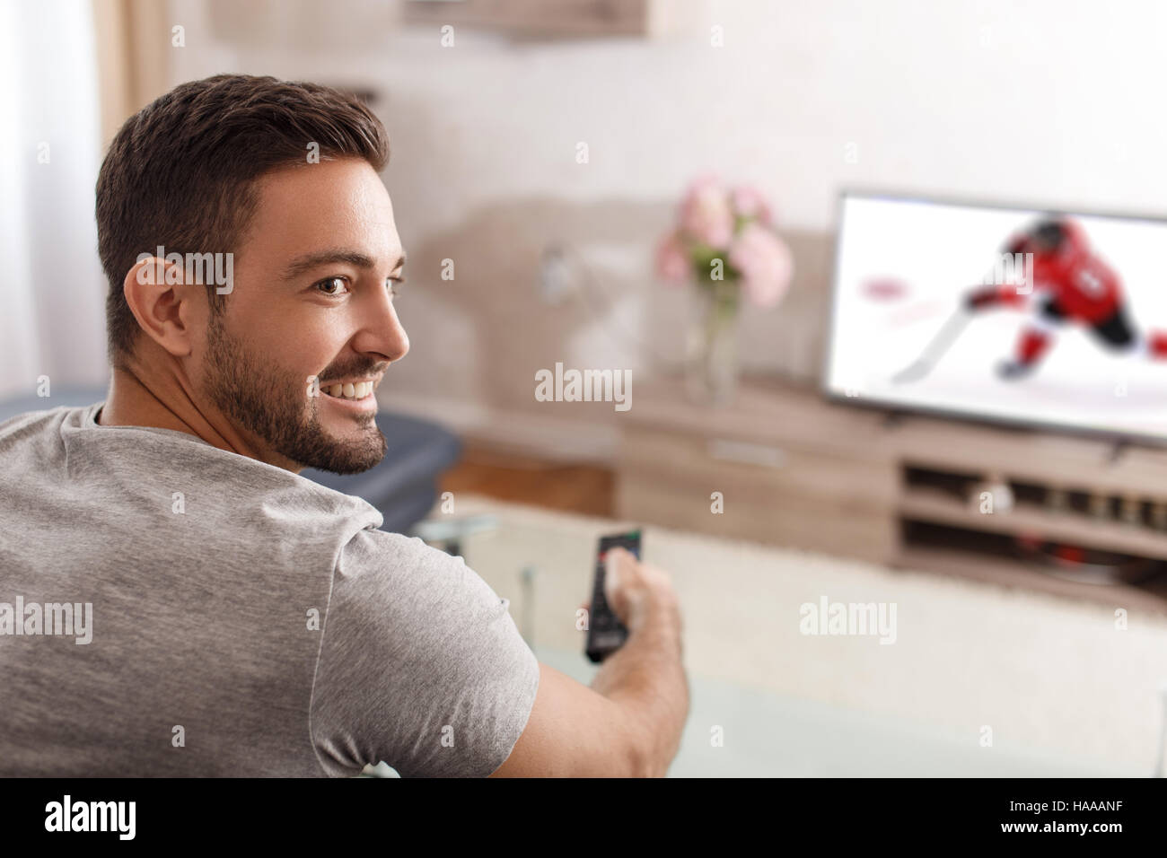 Excited man switch TV to ice hockey by remote control Stock Photo - Alamy